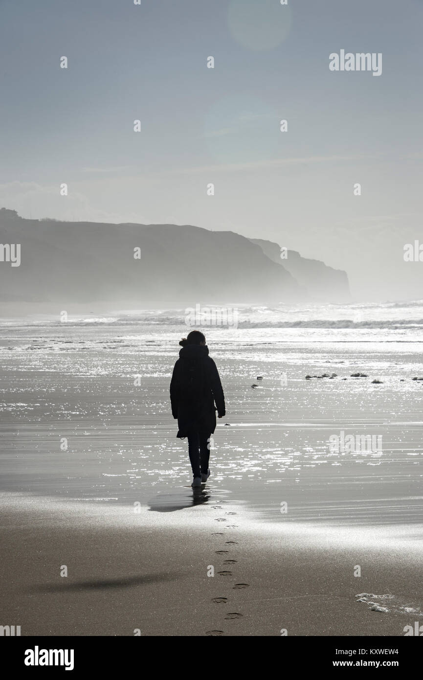 person walking along an empty beach with footsteps in the sand, silver ...