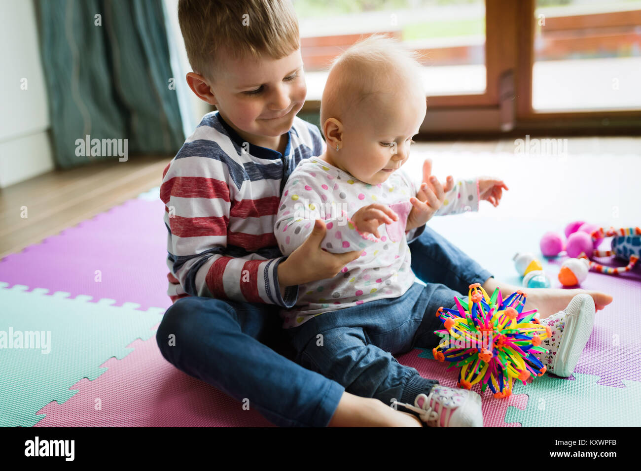 Cute little children playing while sitting on carpet Stock Photo - Alamy