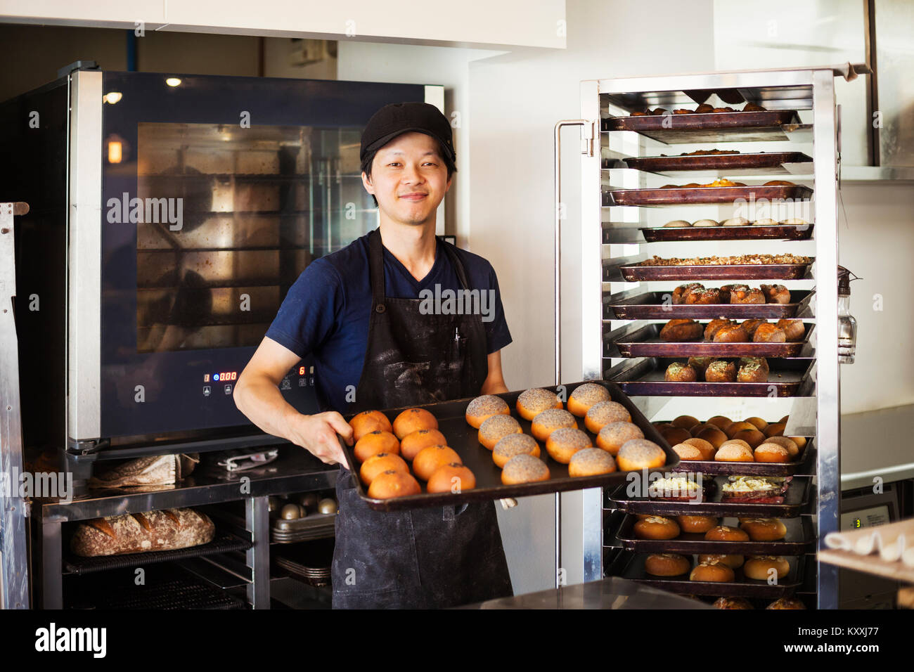 Man working in a bakery, holding large tray with freshly baked rolls ...