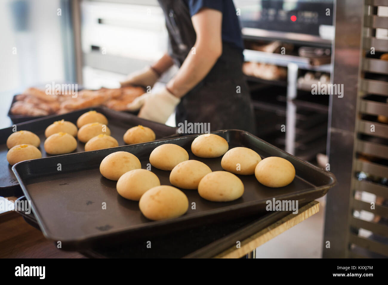 Person working in a bakery, placing freshly baked rolls on large trays ...