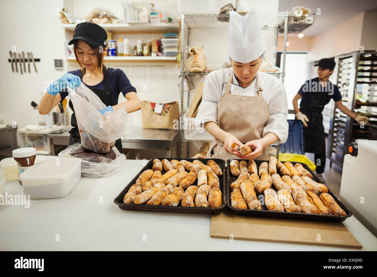Two women and man working in a bakery, preparing freshly baked rolls on ...