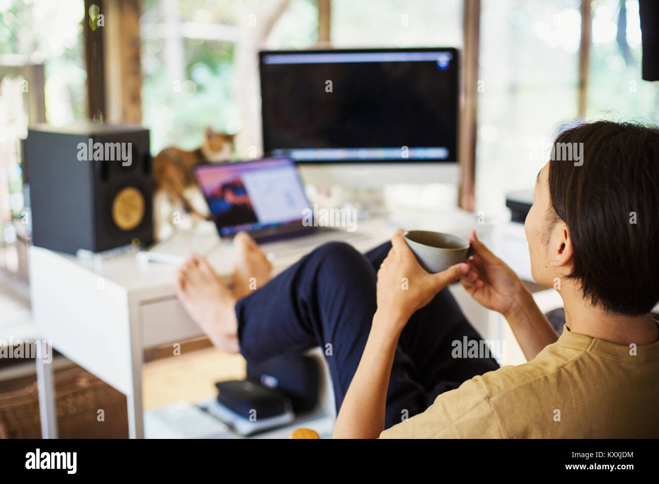 Man sitting indoors at a desk with computer, legs raised, barefoot ...
