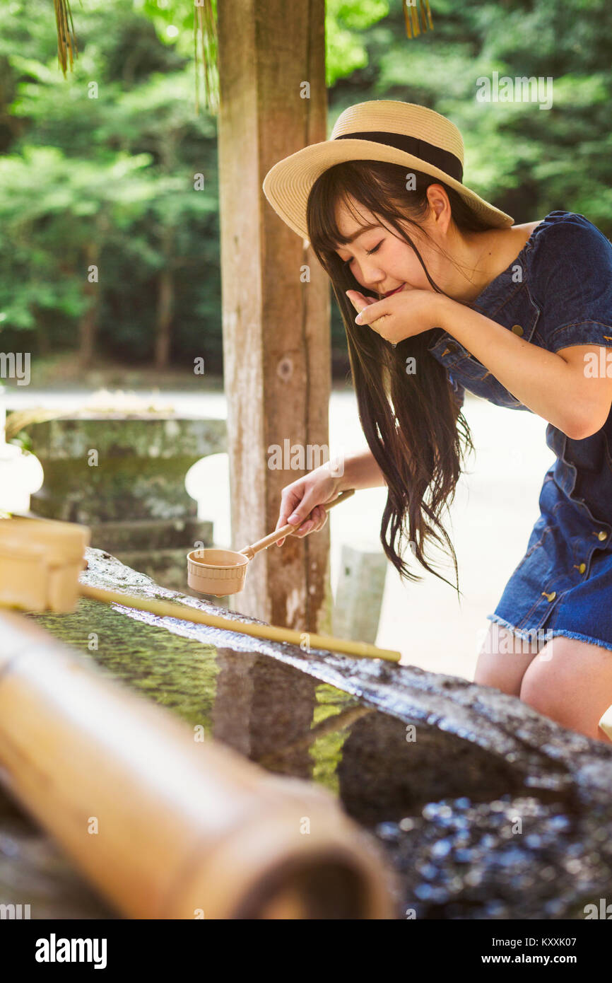 Young woman wearing blue dress and hat using bamboo water hand washing ...
