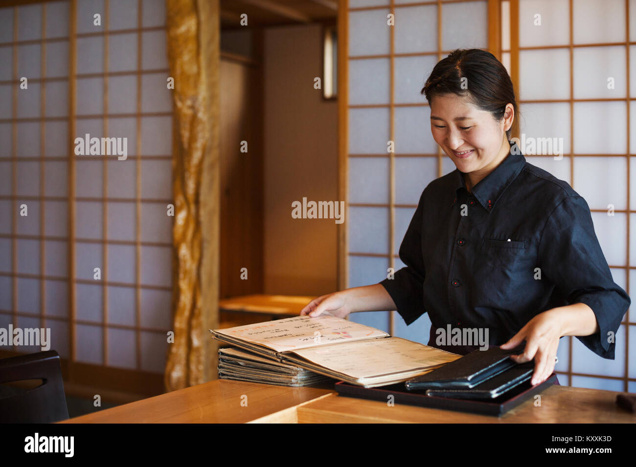 Smiling waitress standing at a counter in a Japanese sushi restaurant ...