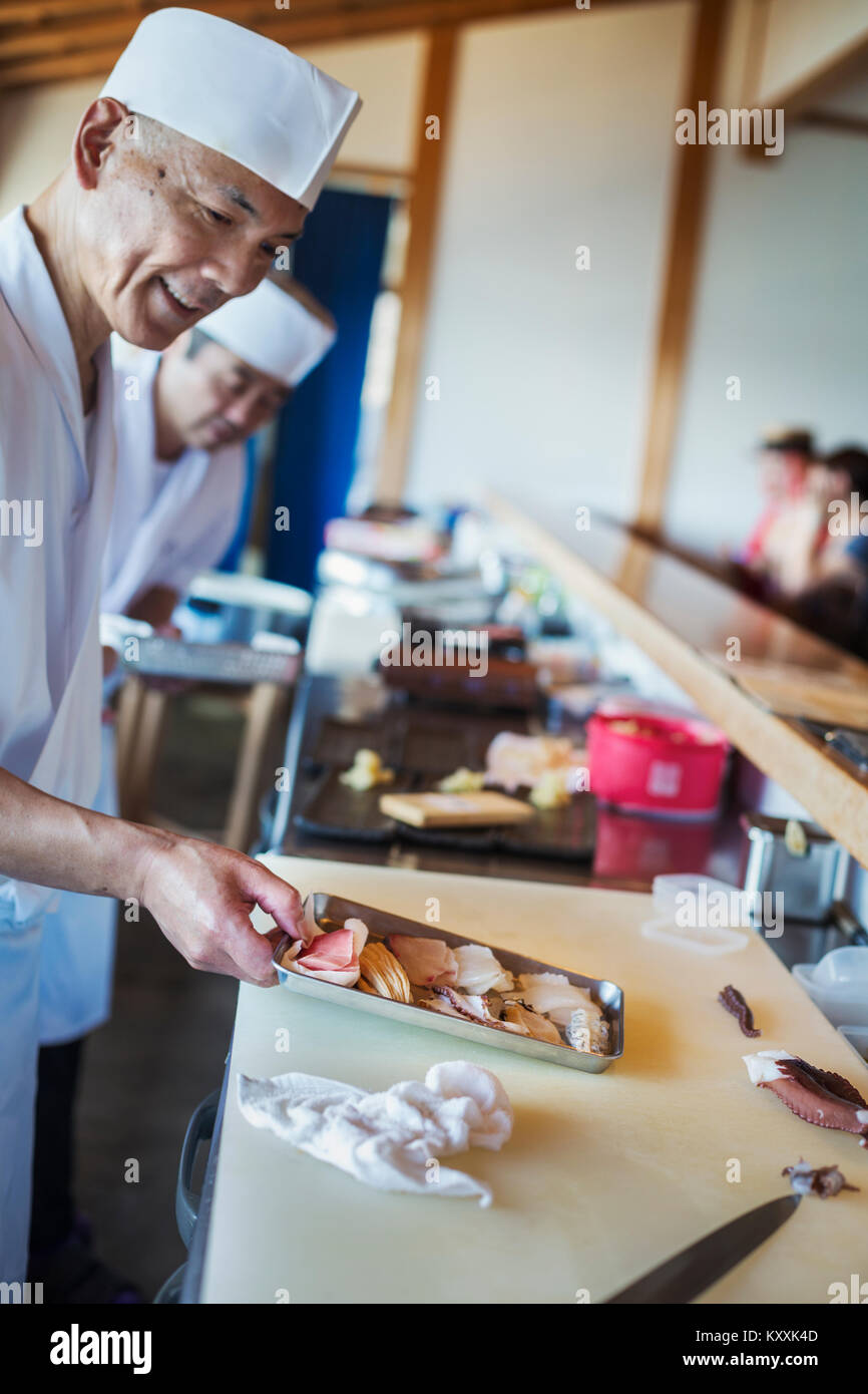 Two chefs working at a counter at a Japanese sushi restaurant, holding ...