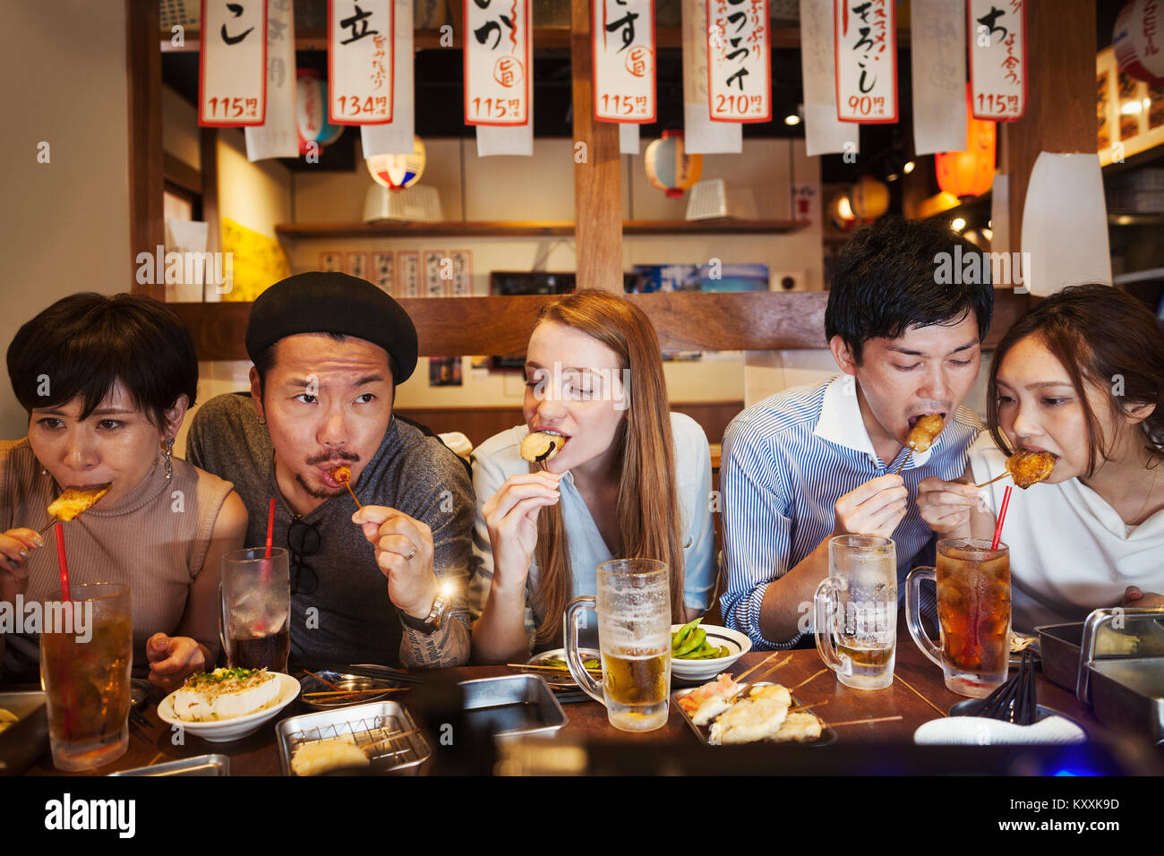 Five people sitting sidy by side at a table in a restaurant, eating ...