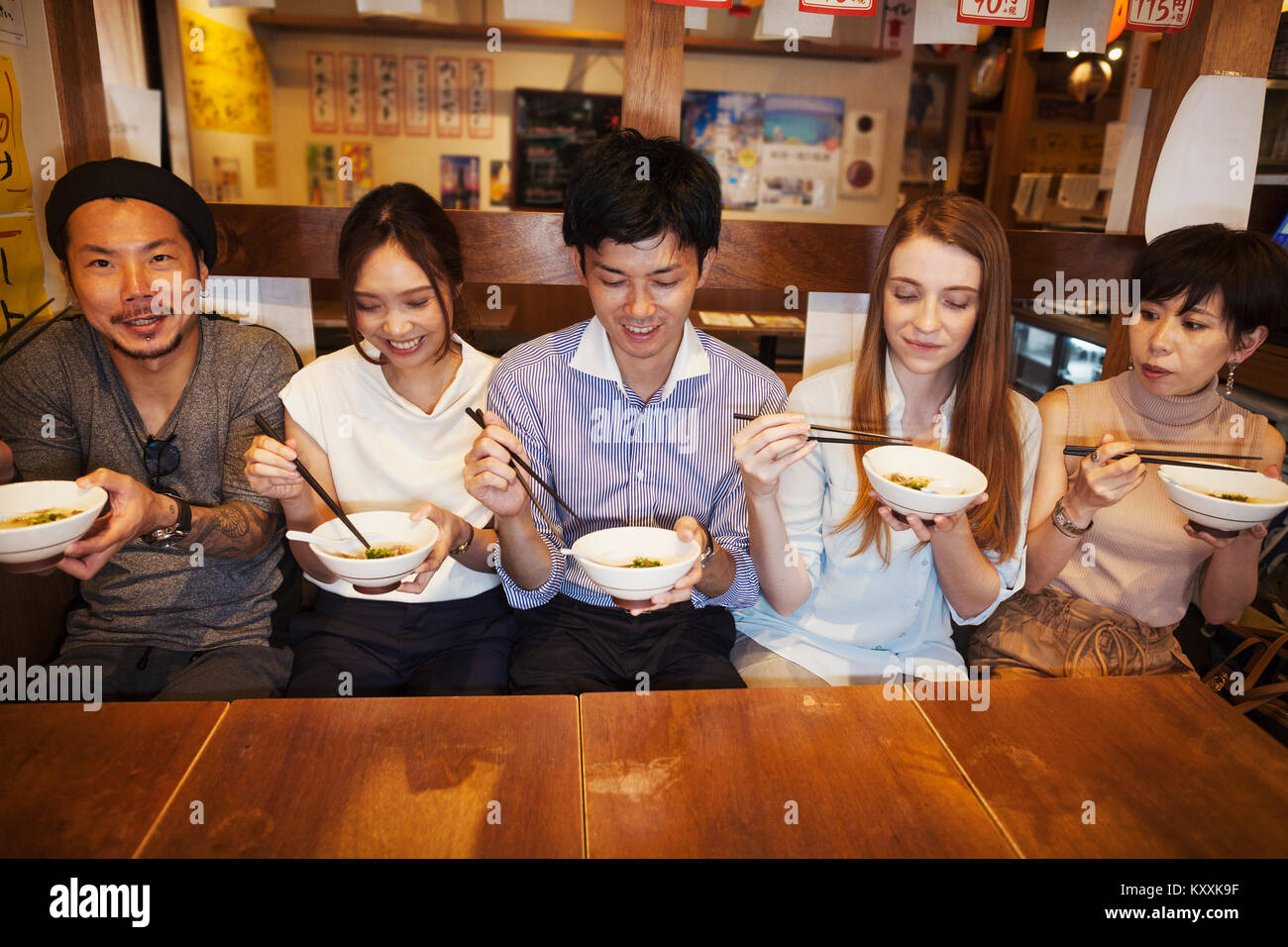 Five people sitting sidy by side at a table in a restaurant, eating ...