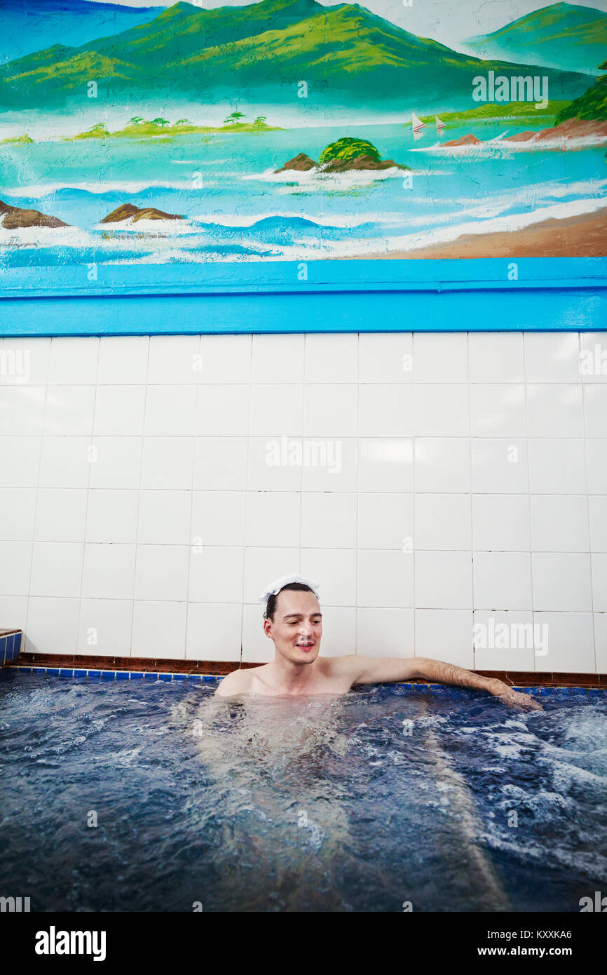 A young Caucasian man seated in a deep pool of moving water in a public ...