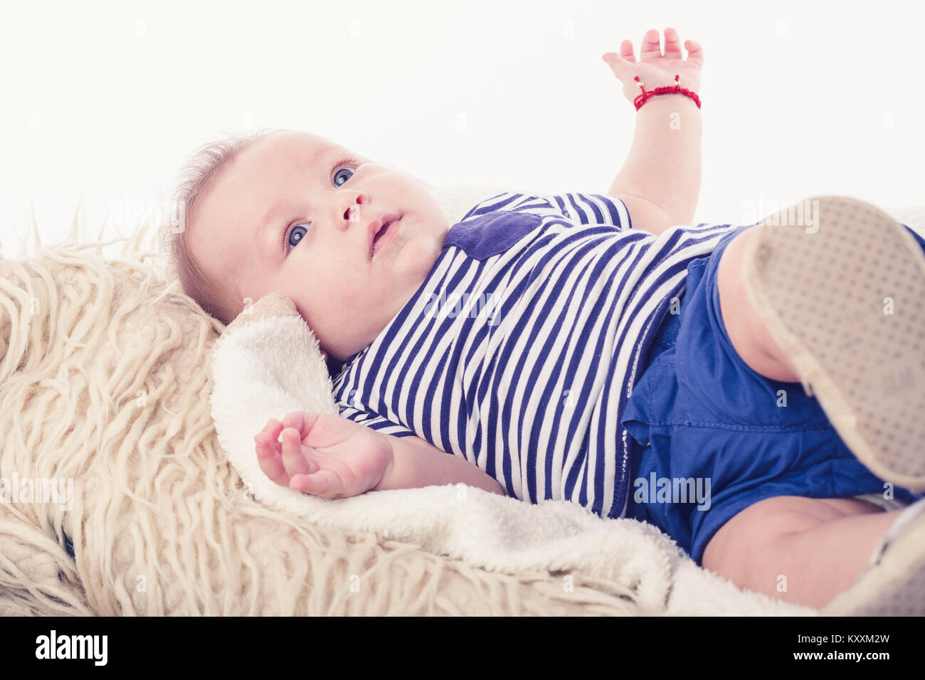 Adorable baby boy with big blue ayes lying on the bed over white ...