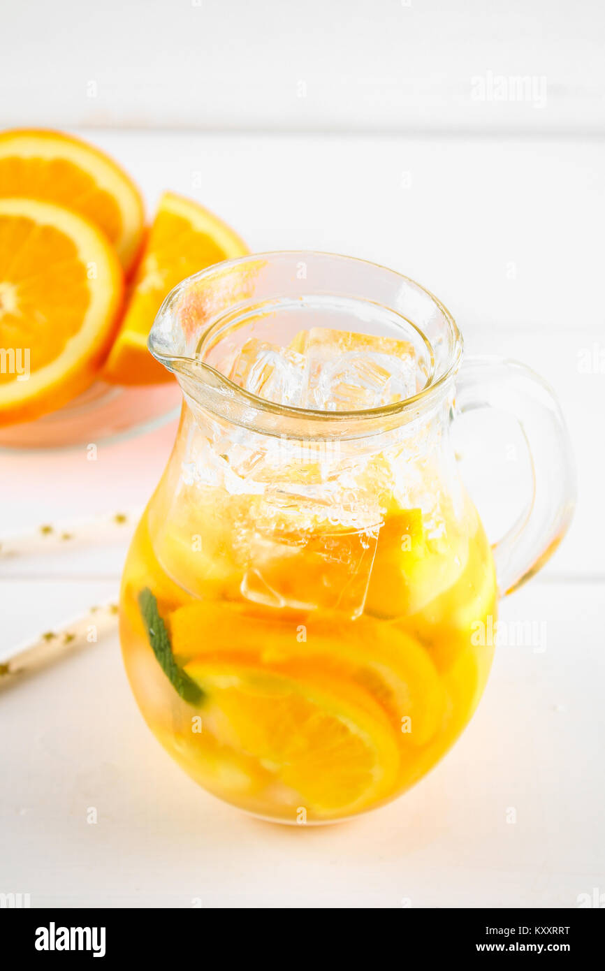 Orange detox water in a jug on a white wooden table. Healthy food ...