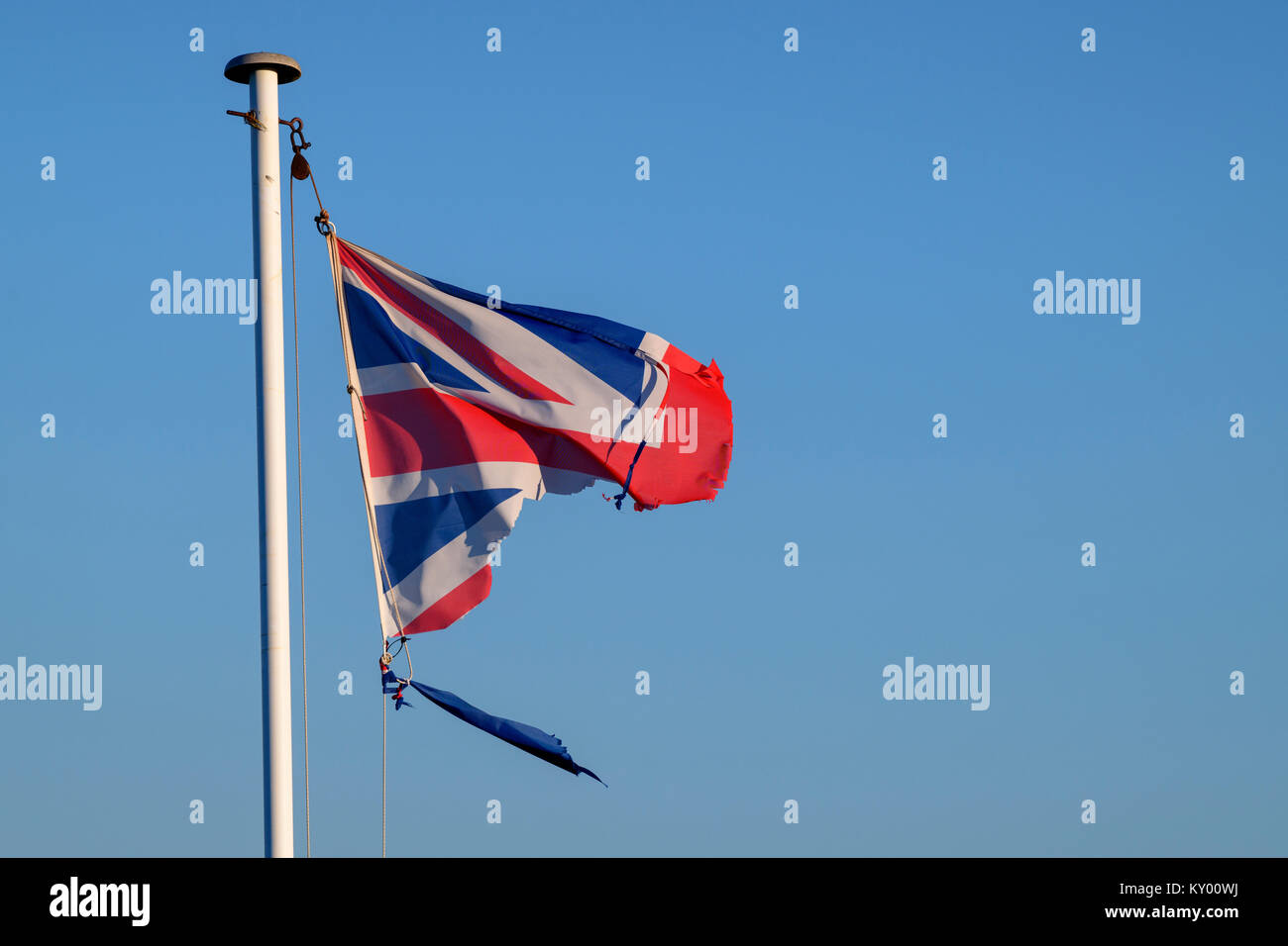 A tattered Union Jack flag fluttering in the wind against a blue sky ...