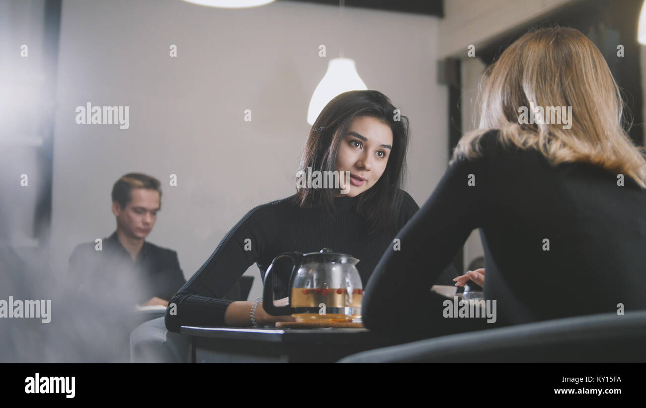 Pretty young woman with black hair talking with girlfriend in the cafe ...