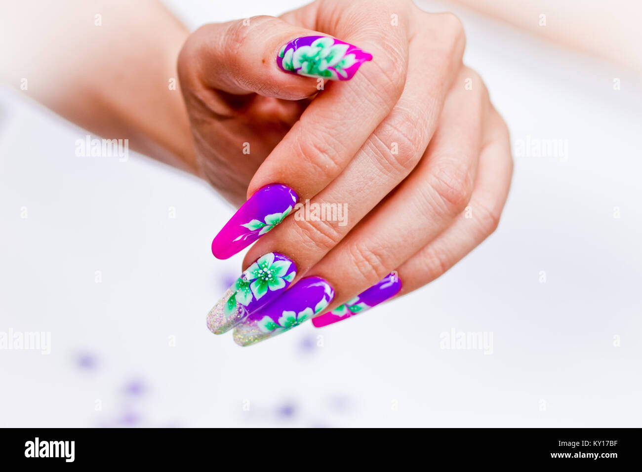 Hand with nails rebuilt and decorated with colorful flowers bring blue ...