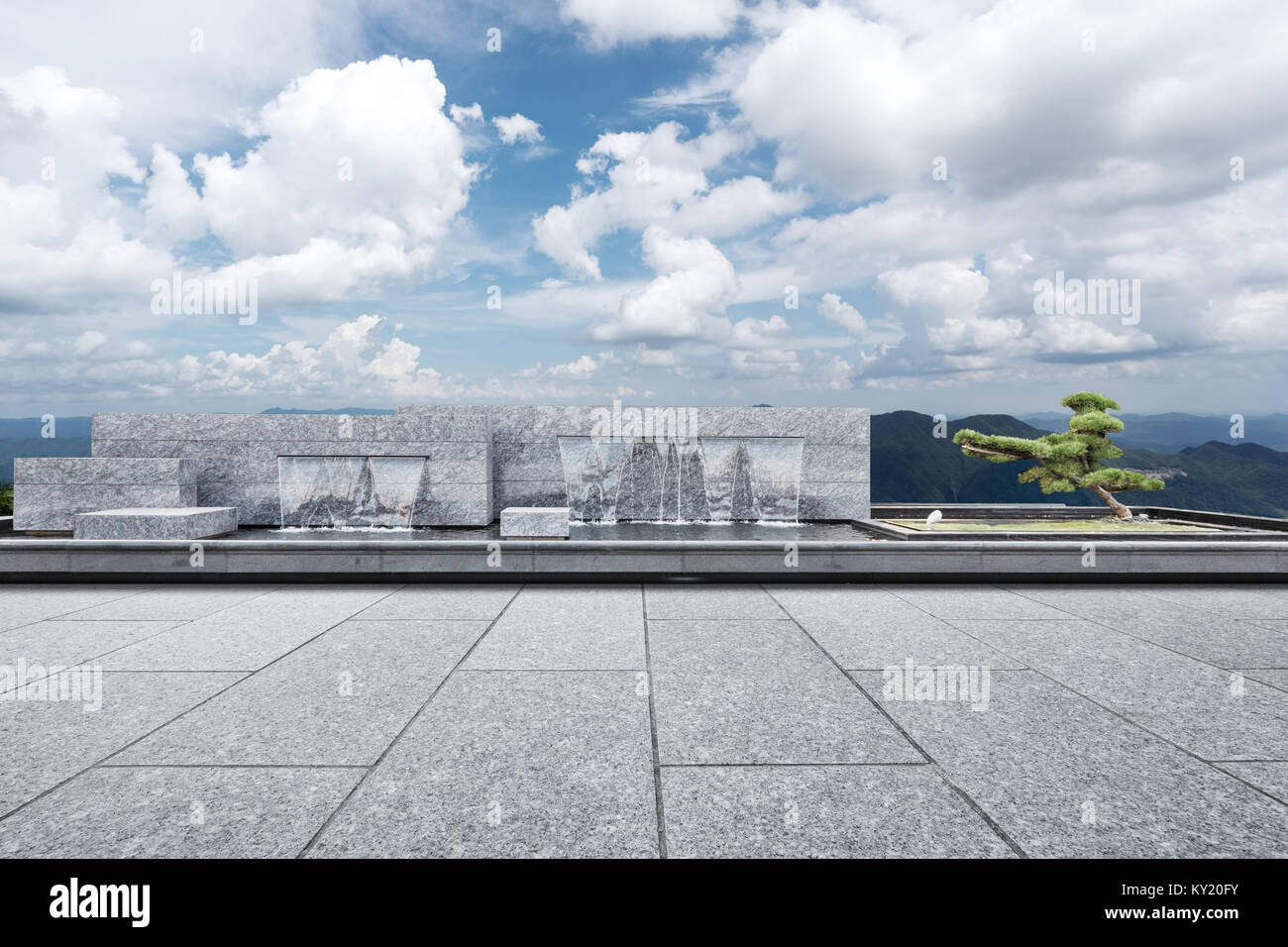 empty marble square with artificial waterfall and green hill in blue ...