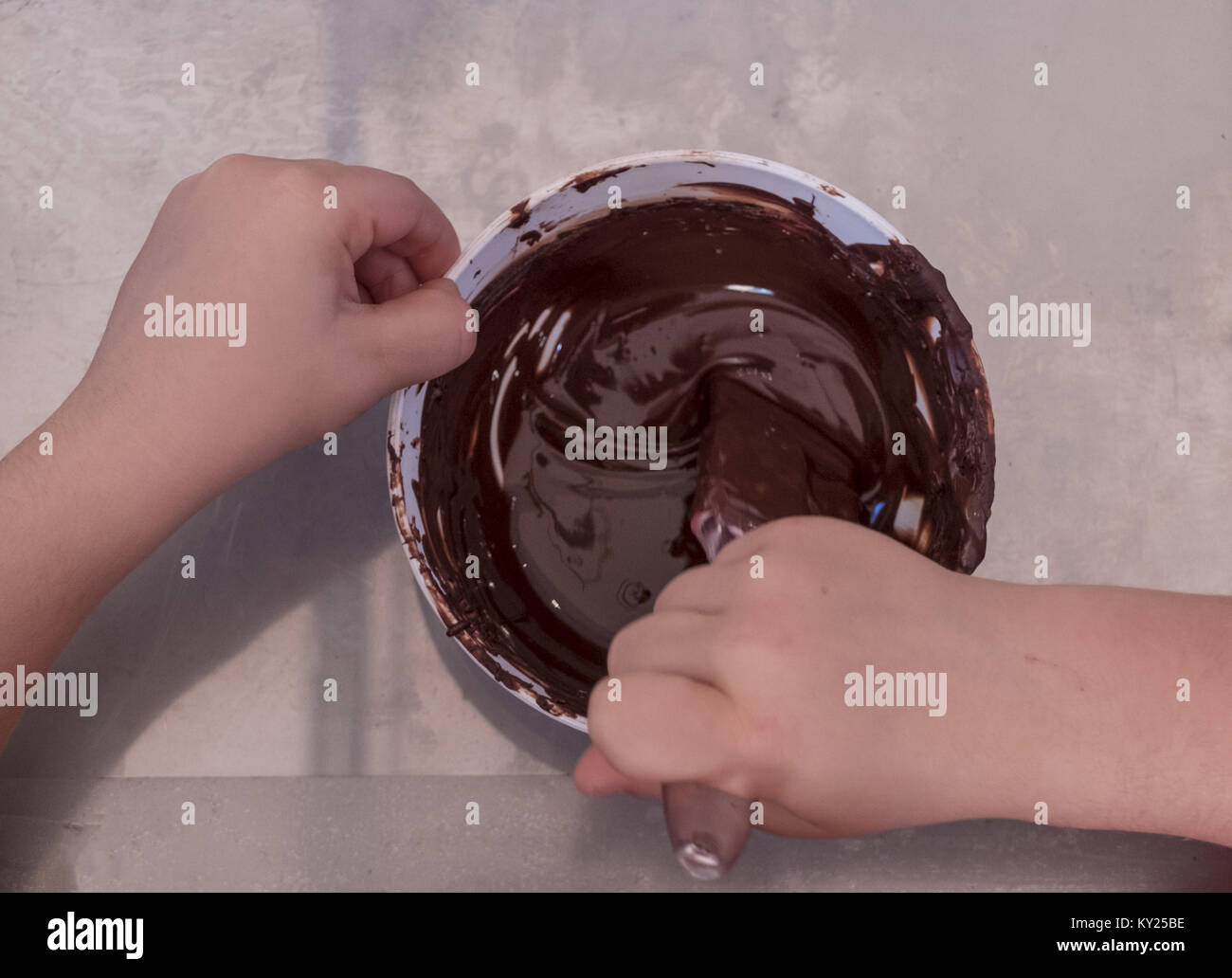 hands of a child play the pastry chef mixing chocolate in a bowl before ...