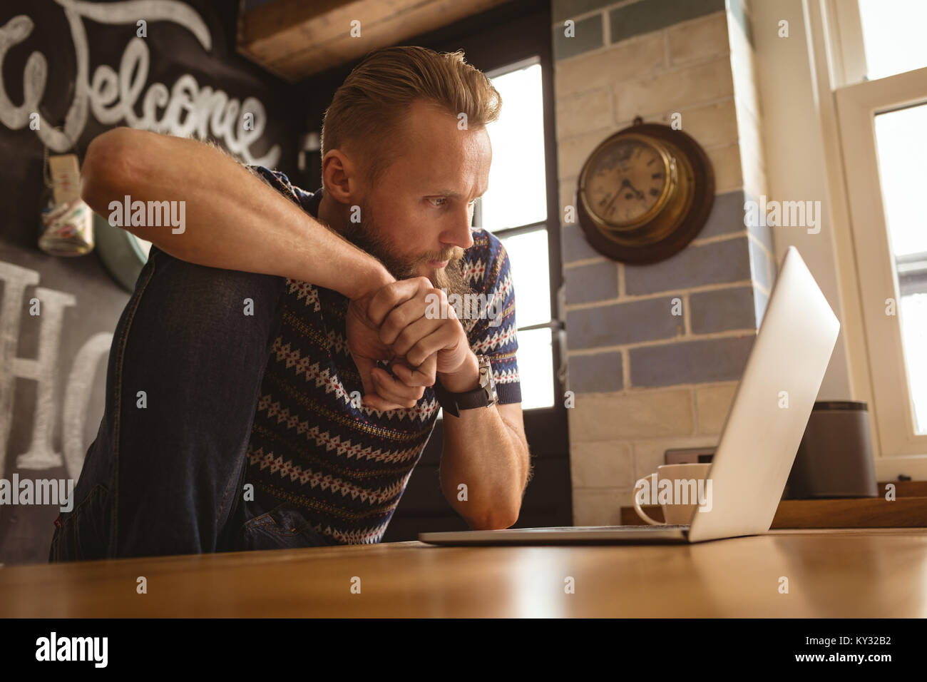 Man sitting on table looking at his laptop Stock Photo - Alamy