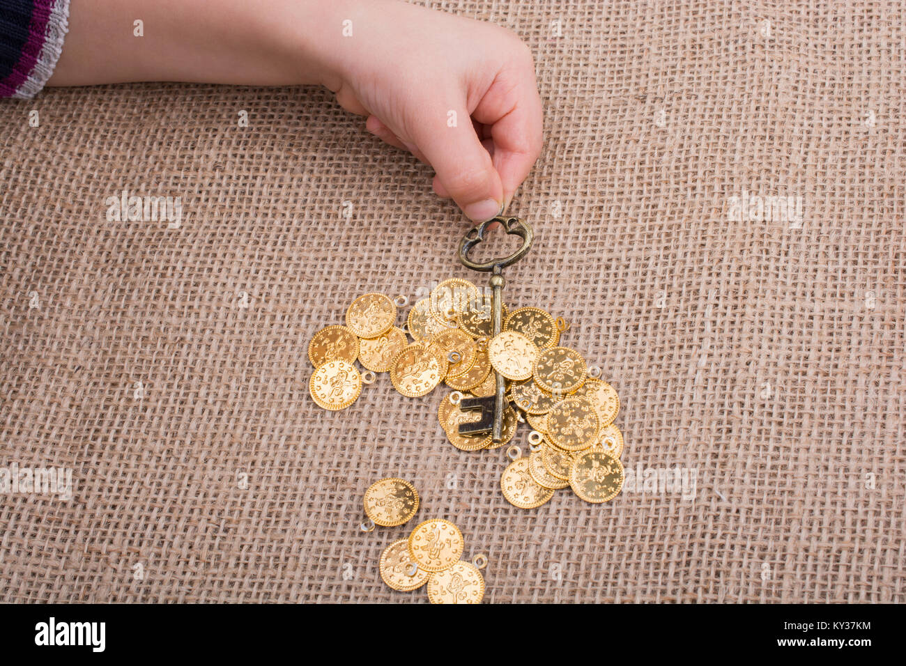 Hand holding a retro styled key over fake gold coins Stock Photo - Alamy