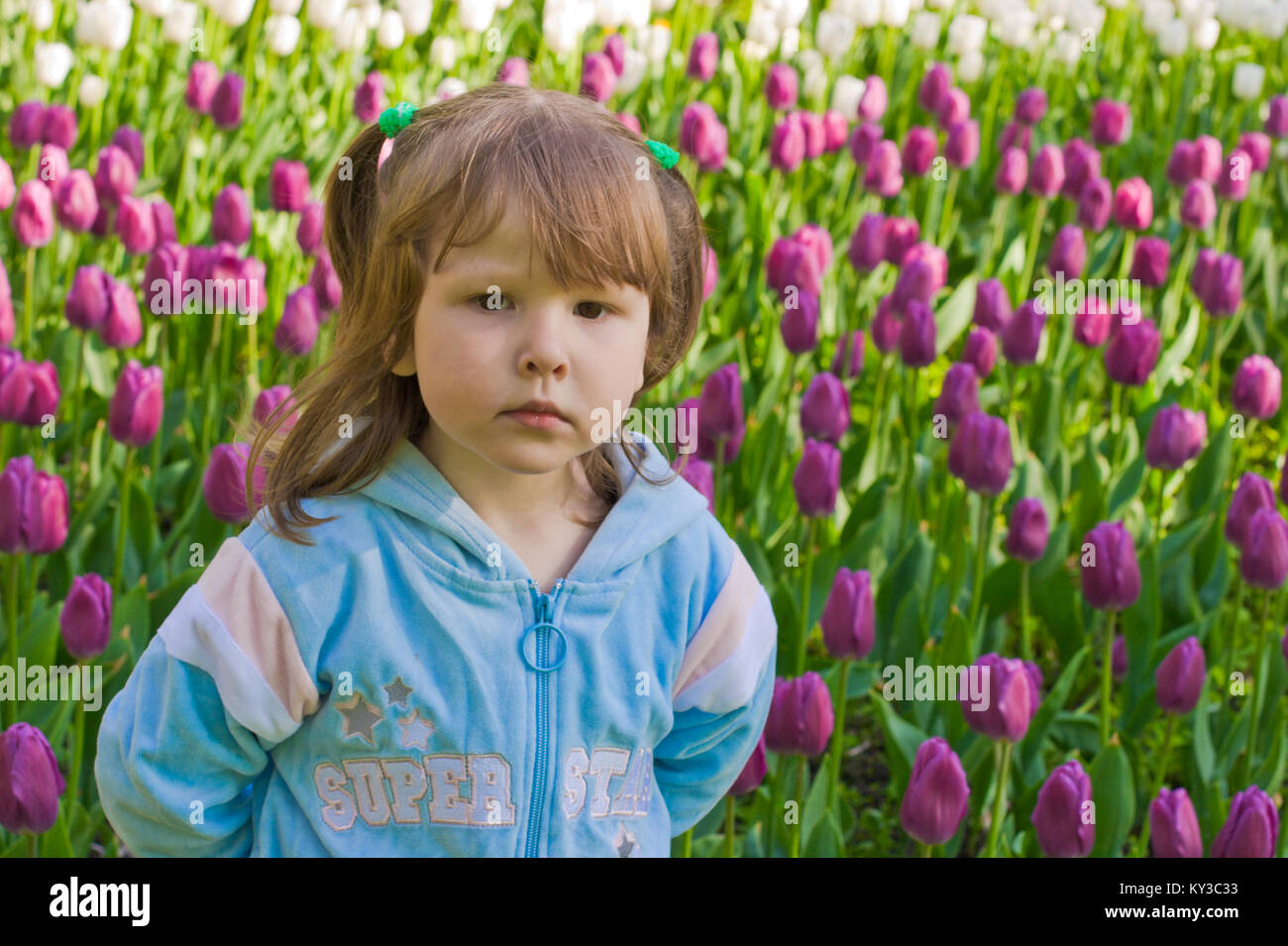 Portrait of little girl with sad face over white and purple tulips ...
