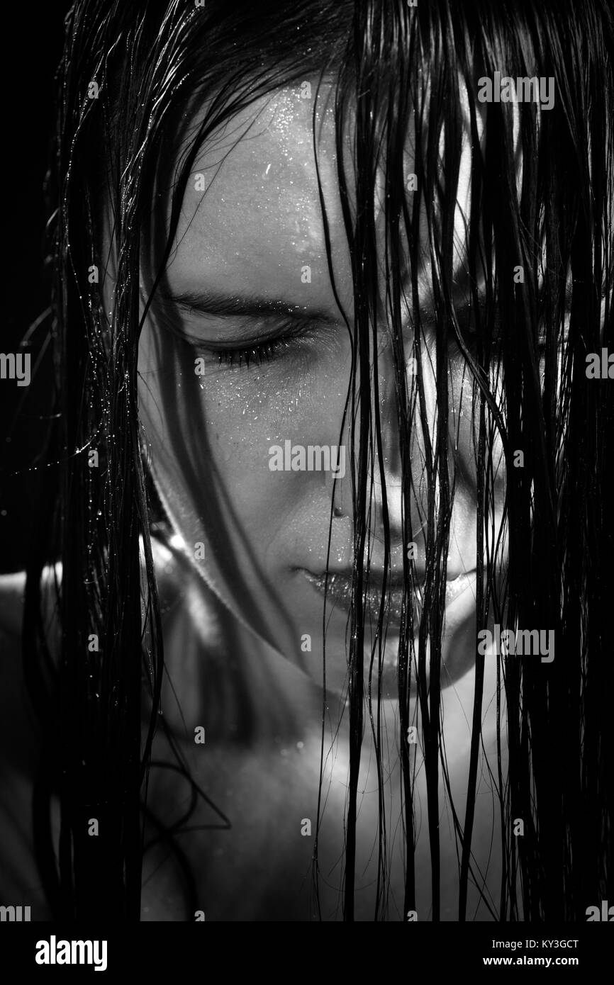 serious sad woman with wet black hair close her eyes in dark ...