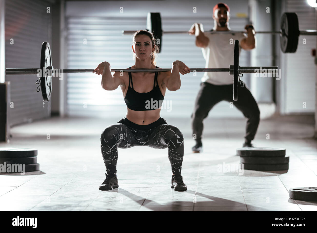 Young muscular couple doing a high pull exercise with barbell on cross ...