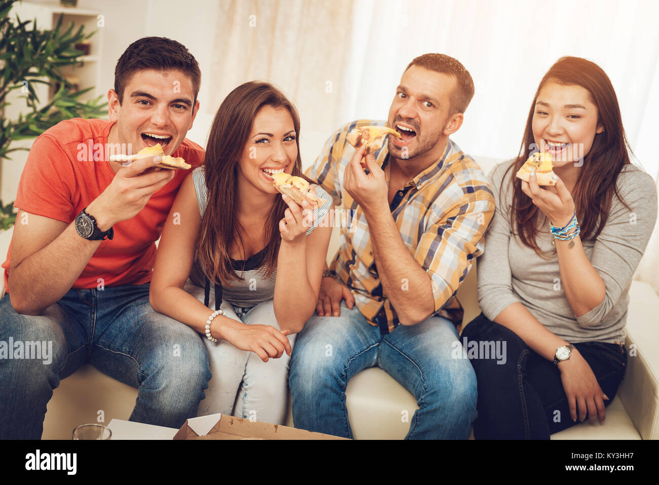 Four cheerful friends hanging out in an apartment. They are eating ...