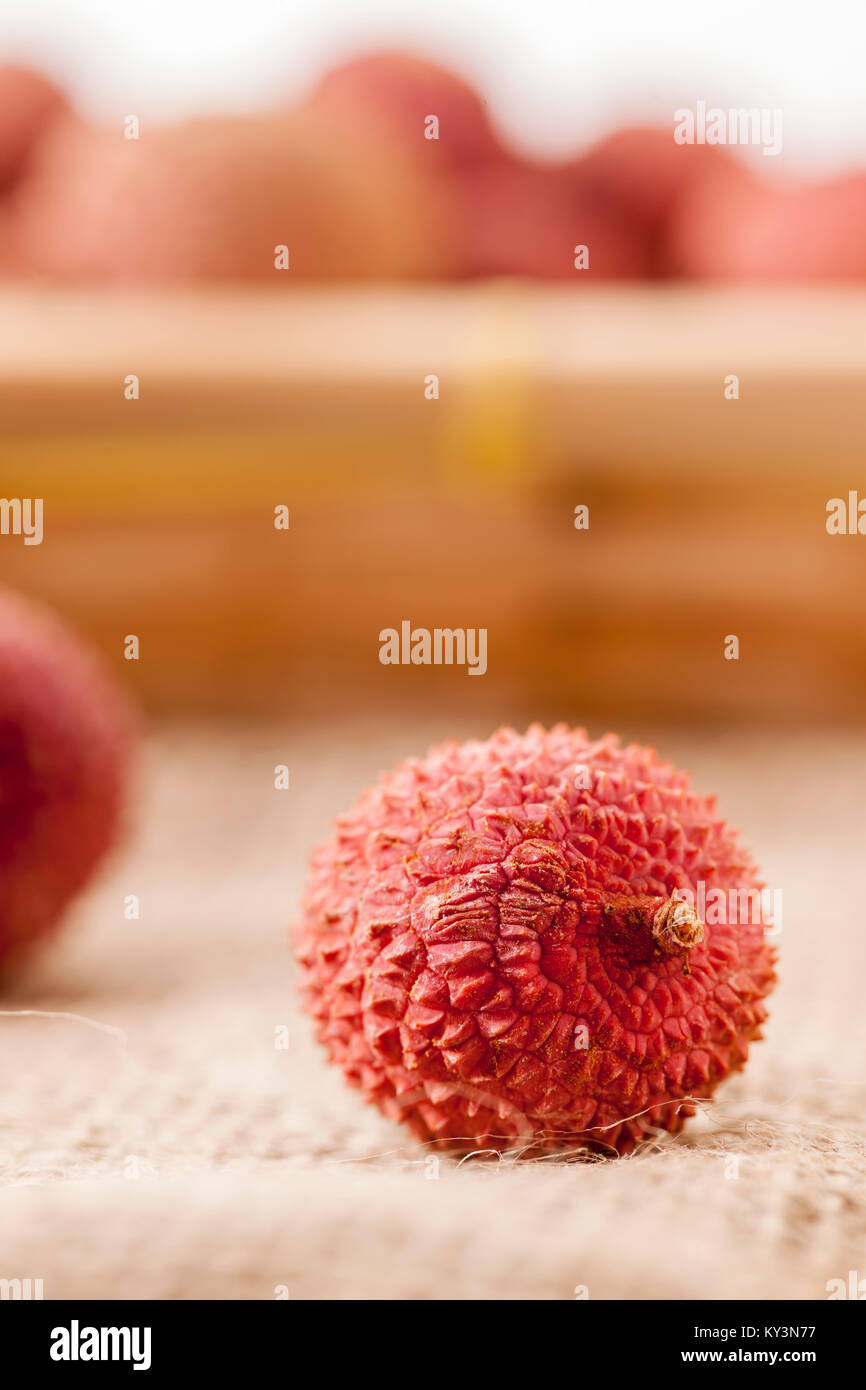 Detail view of a single lychee fruit on rough sackcloth fabric in front ...