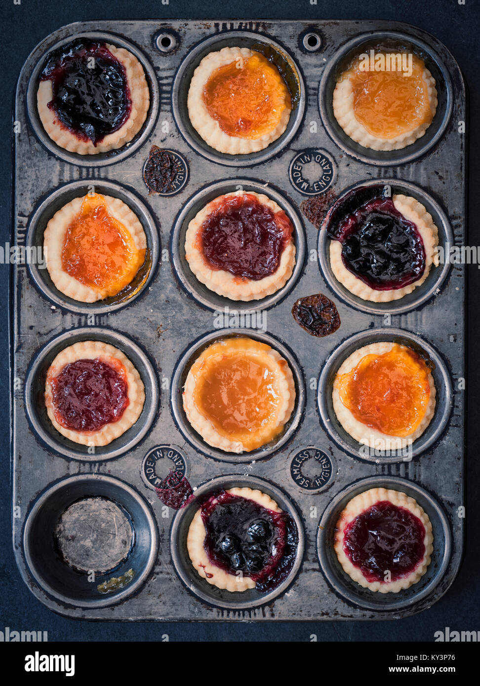 Cooked homemade jam tarts in a baking tray on slate. Vintage filter ...