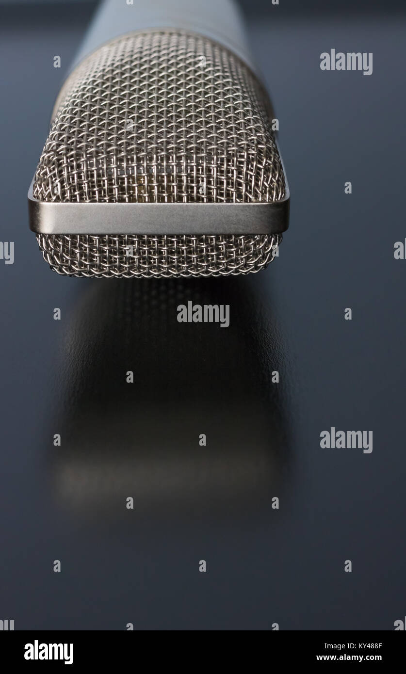 A silver condenser microphone is placed on a shiny surface. The object ...
