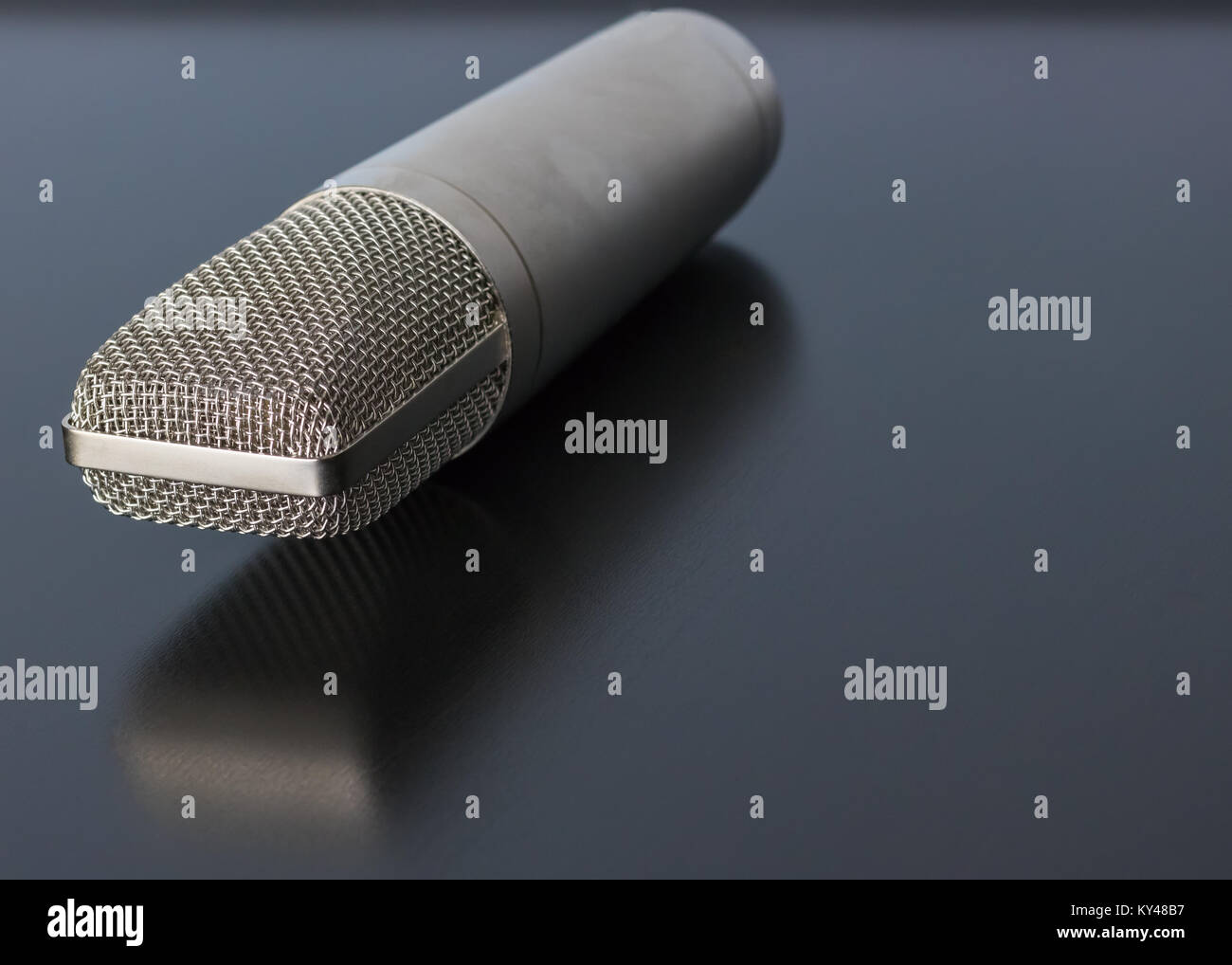 A silver condenser microphone is placed on a shiny surface. The object ...