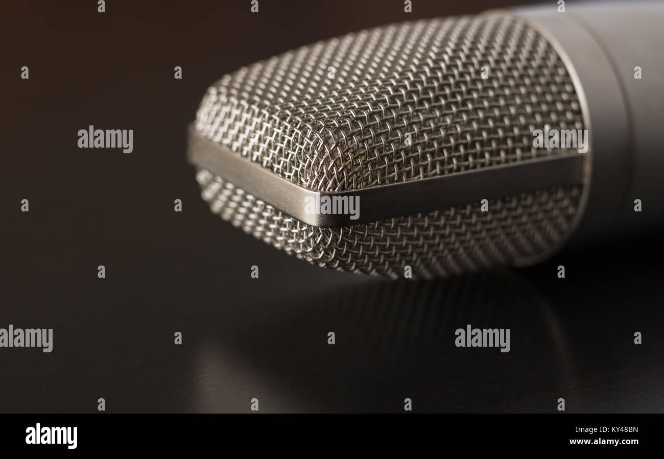 A silver condenser microphone is placed on a shiny surface. The object ...