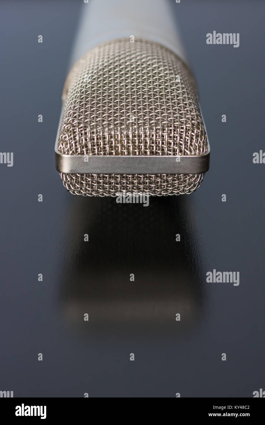 A silver condenser microphone is placed on a shiny surface. The object ...