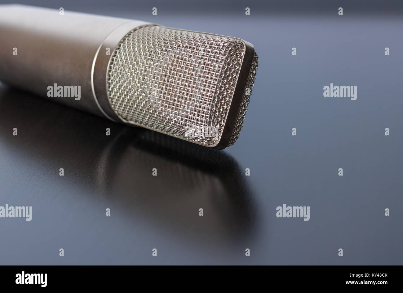 A silver condenser microphone is placed on a shiny surface. The object ...