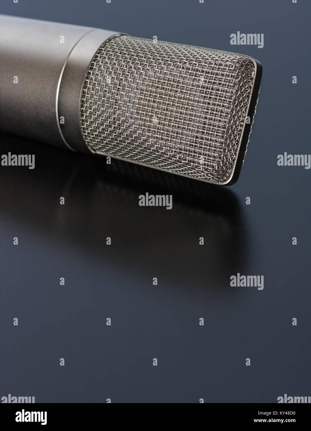 A silver condenser microphone is placed on a shiny surface. The object ...