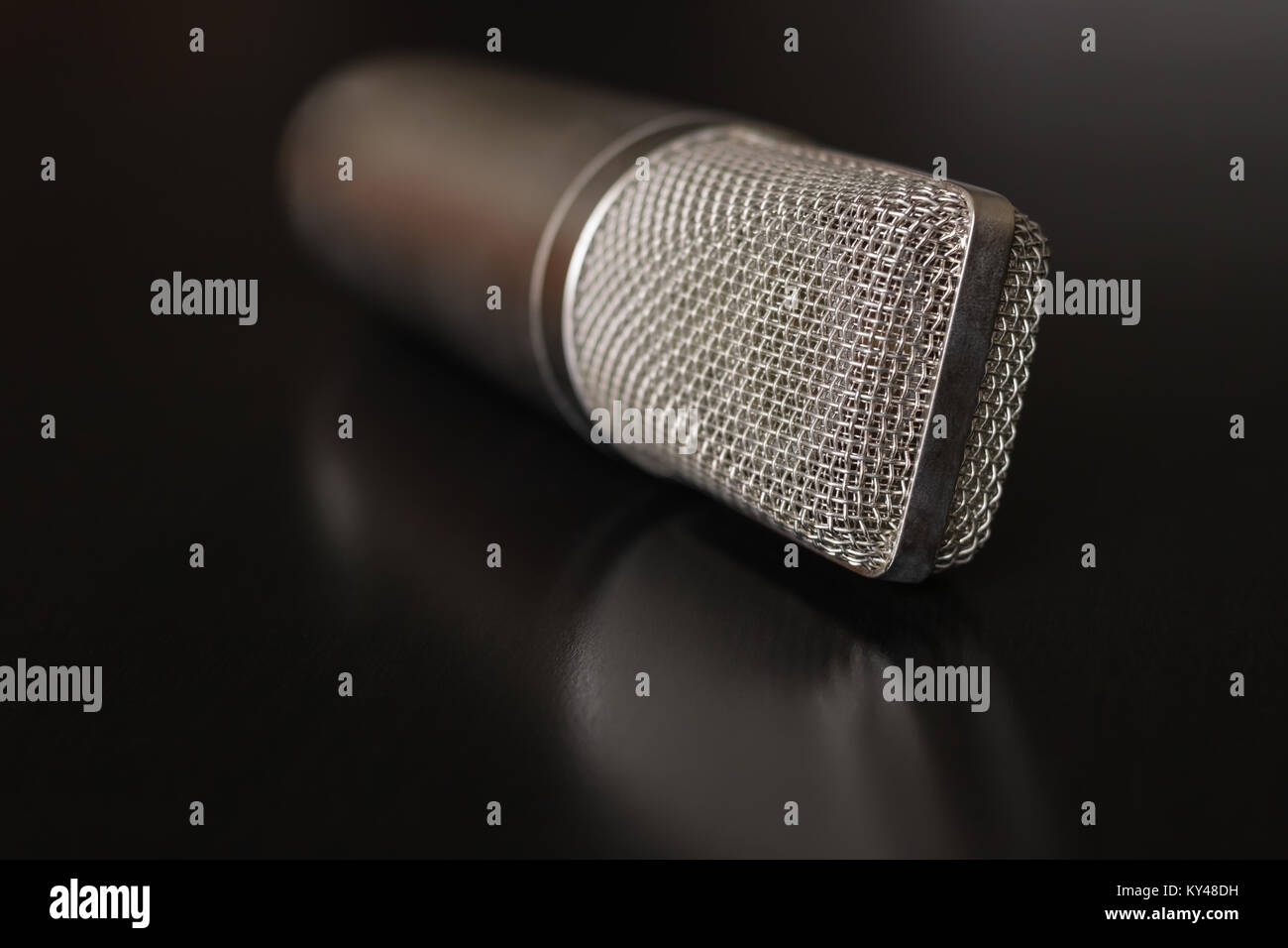 A silver condenser microphone is placed on a shiny surface. The object ...