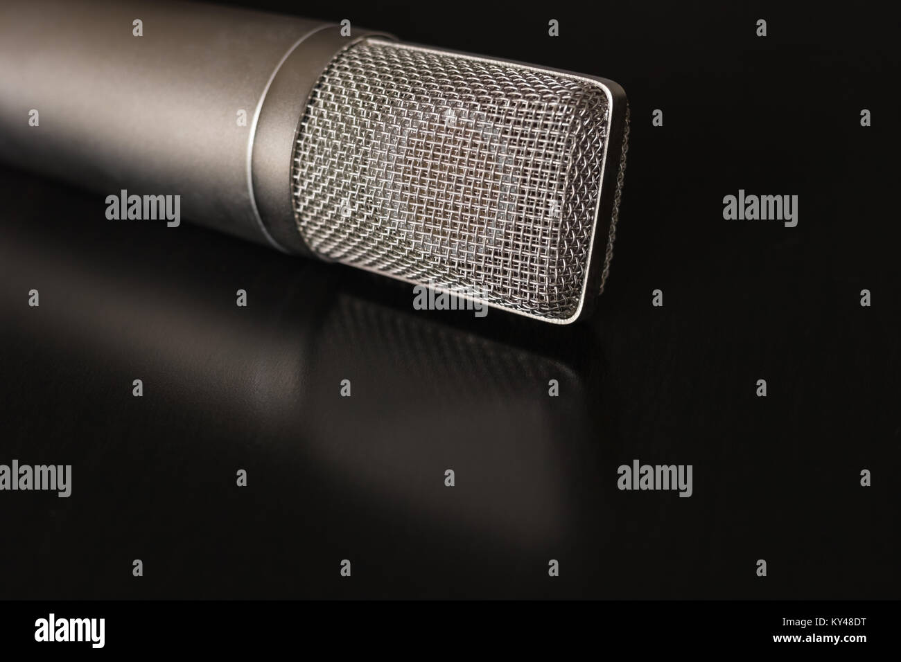 A silver condenser microphone is placed on a shiny surface. The object ...