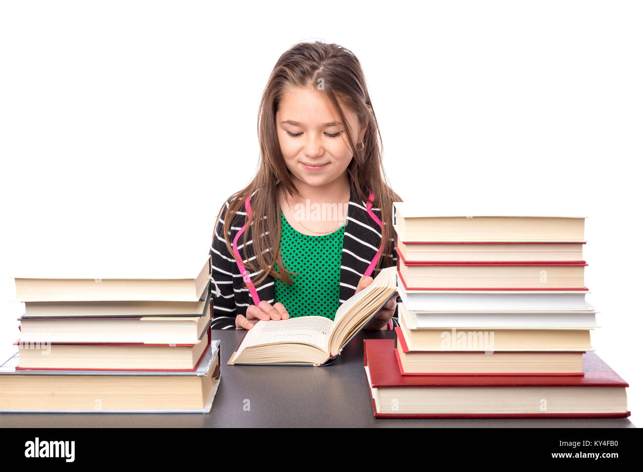 Adorable school girl reading a book at her desk isolated on white ...