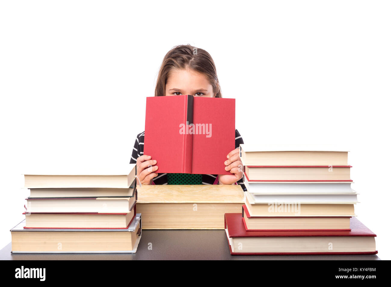 Beautiful school girl covering her face with a book sitting at desk ...