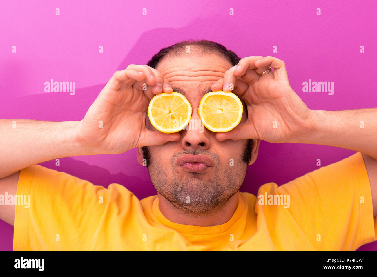 Portrait of a man holding two sliced lemons in his eyes and making ...