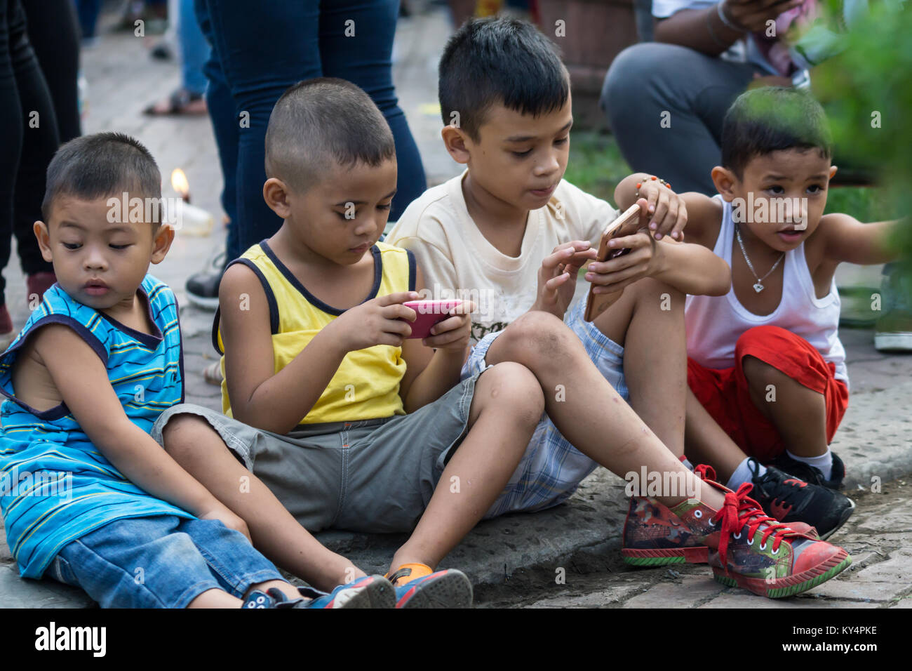 Filipino boys sitting on roadside using smartphones together in a ...