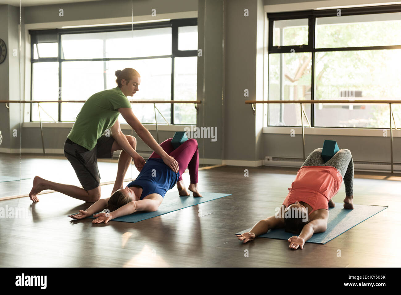 Trainer assisting women in practicing yoga Stock Photo - Alamy