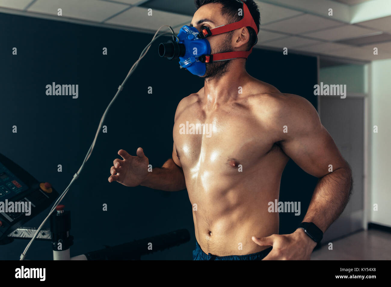 Muscular athlete with mask running on treadmill in gym for monitoring ...