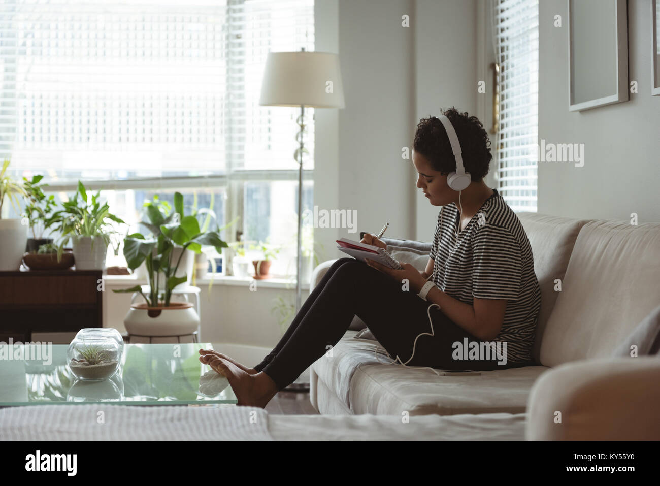 Woman listening to music while writing in notebook Stock Photo - Alamy