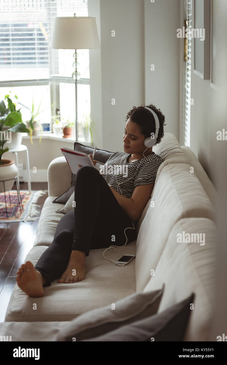 Woman listening to music while writing in notebook Stock Photo - Alamy