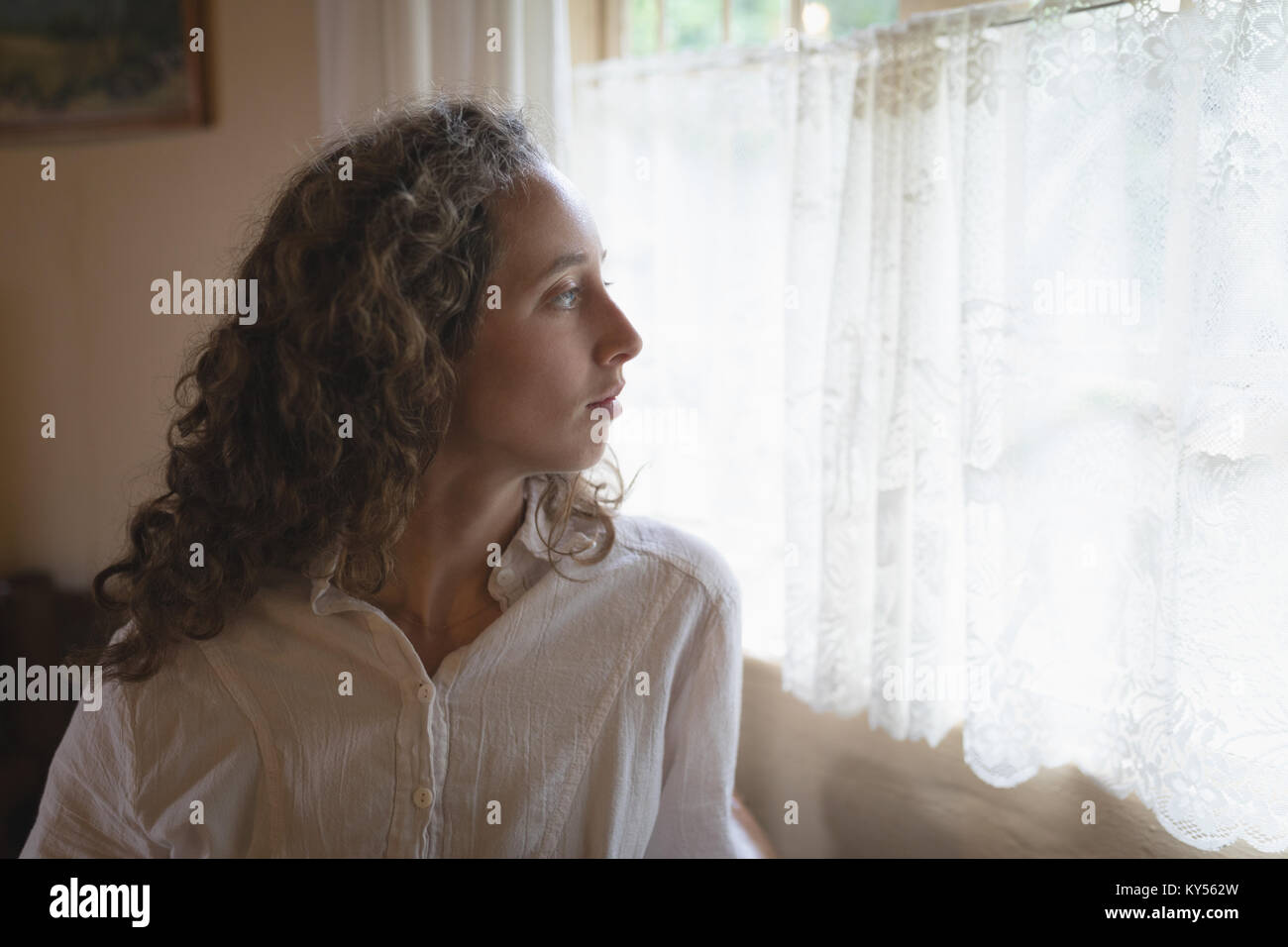 Woman looking through window in living room Stock Photo - Alamy
