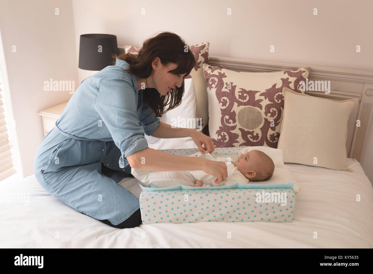 Cute little baby getting dressed by her mother on bed in the bedroom ...