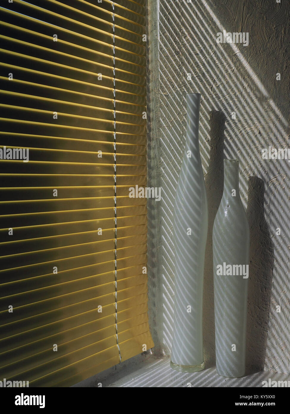Golden half-open blinds cast slanting parallel shadows on the white ...