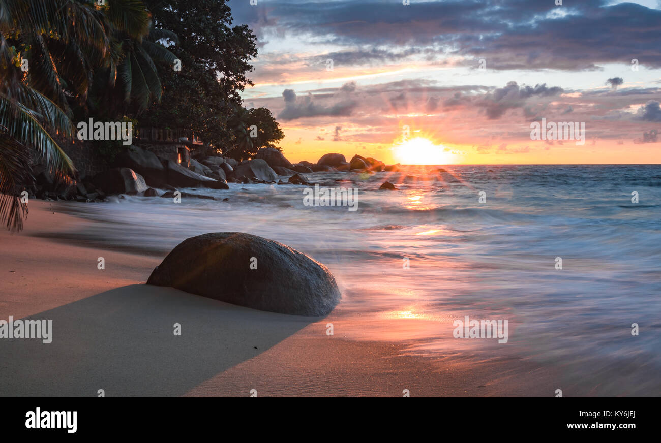 Sunset at Mahé in the Seychelles. Beach photo with waves, sun, rock and ...