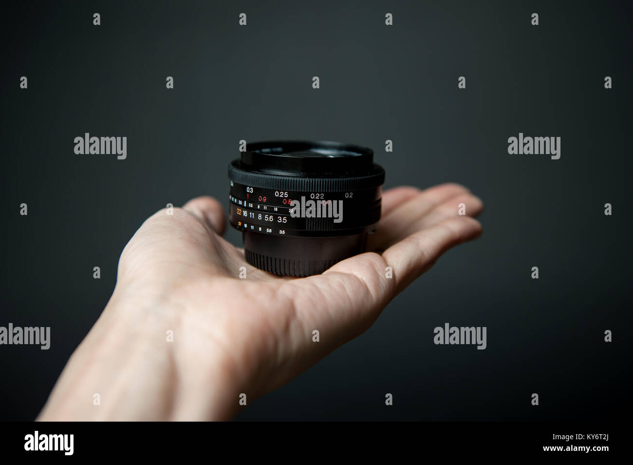 man's hand holding a camera lens on a black background Stock Photo - Alamy