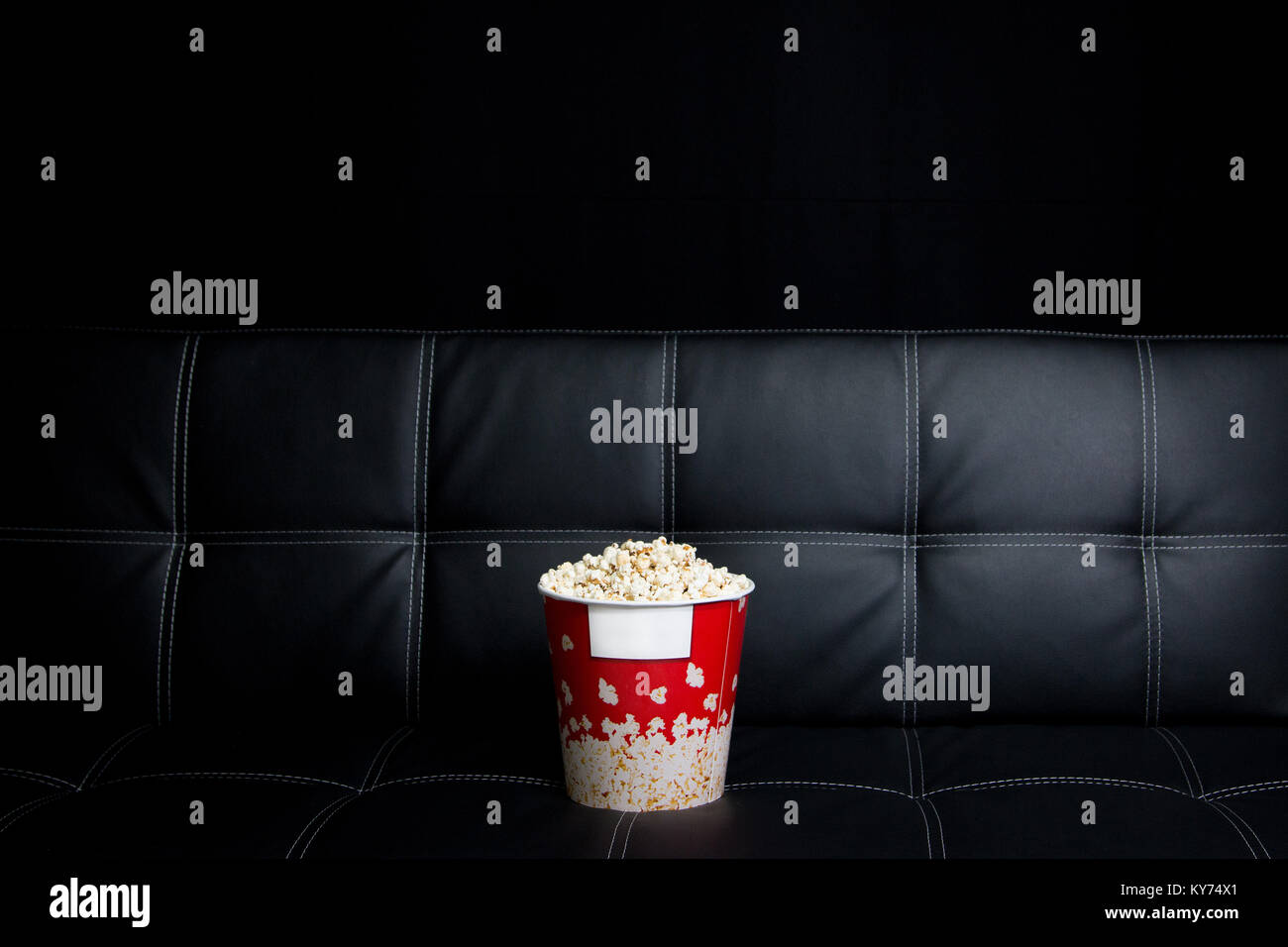 Scene of a popcorn box on a black leather couch with black background ...