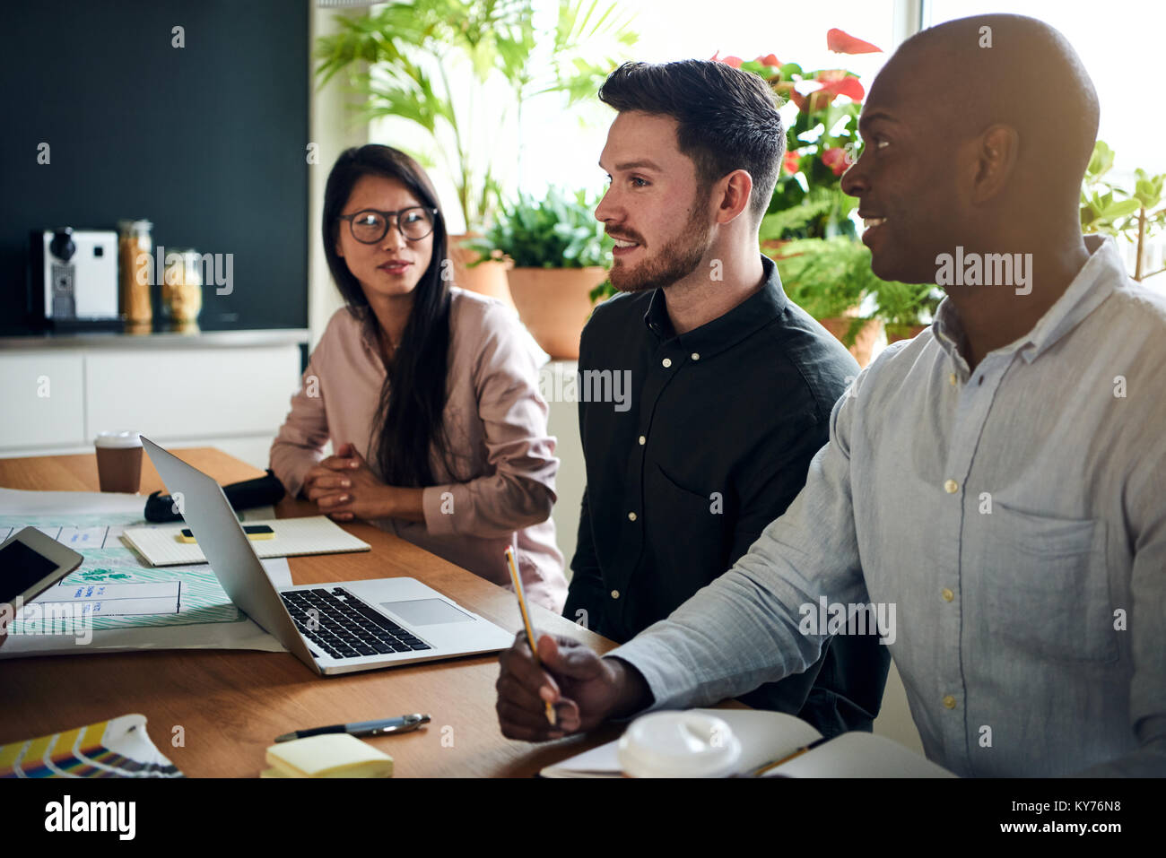 Three diverse work colleagues smiling and talking while sitting ...